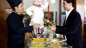 Uma mesa de buffet com várias estações de comida e um garçom servindo.