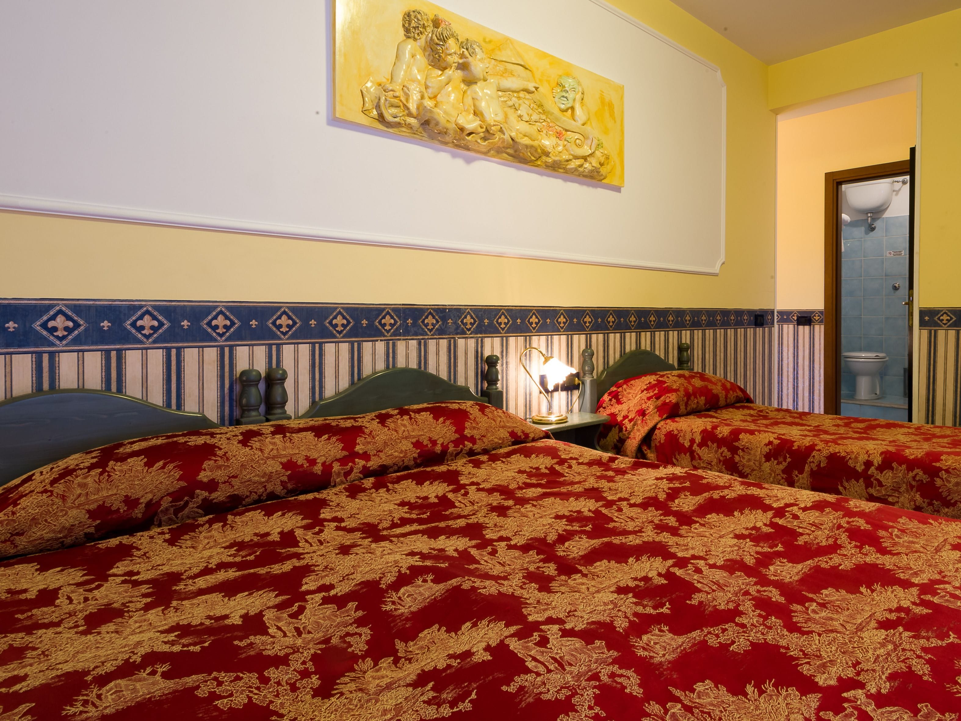 Quarto de hotel com duas camas, um quadro na parede e um banheiro visível através de uma porta aberta.