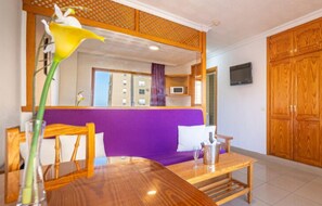 Quarto com mesa de jantar de madeira, sofá roxo e armários de madeira.
