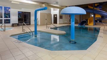 Piscina interna com um escorregador azul, prancha de mergulho e piso ladrilhado.