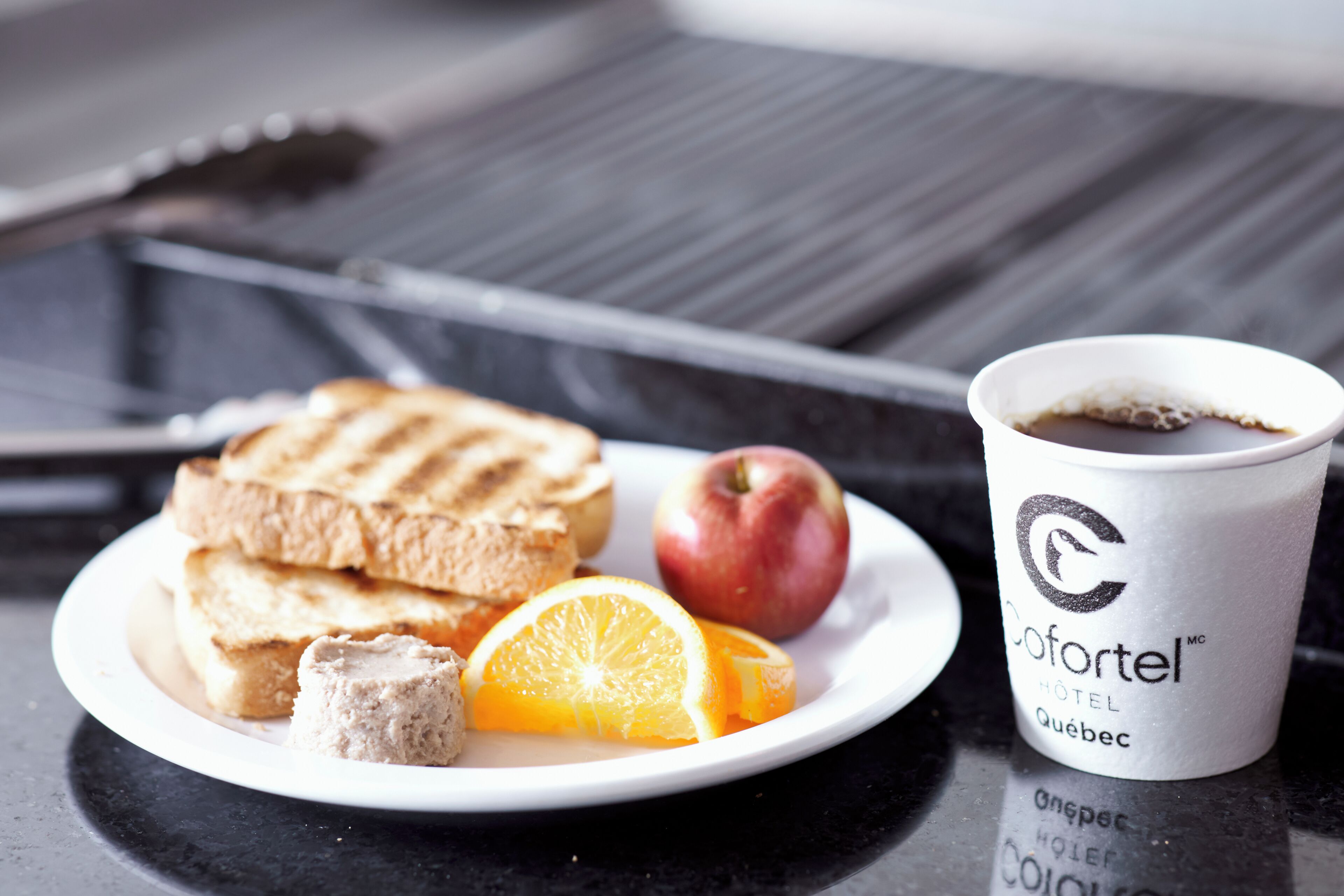 Um prato com torradas, uma maçã e uma fatia de laranja, e uma xícara de café com o logotipo de um hotel.