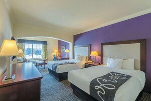 Quarto de hotel com duas camas, uma mesa, uma cadeira e uma janela com cortinas.