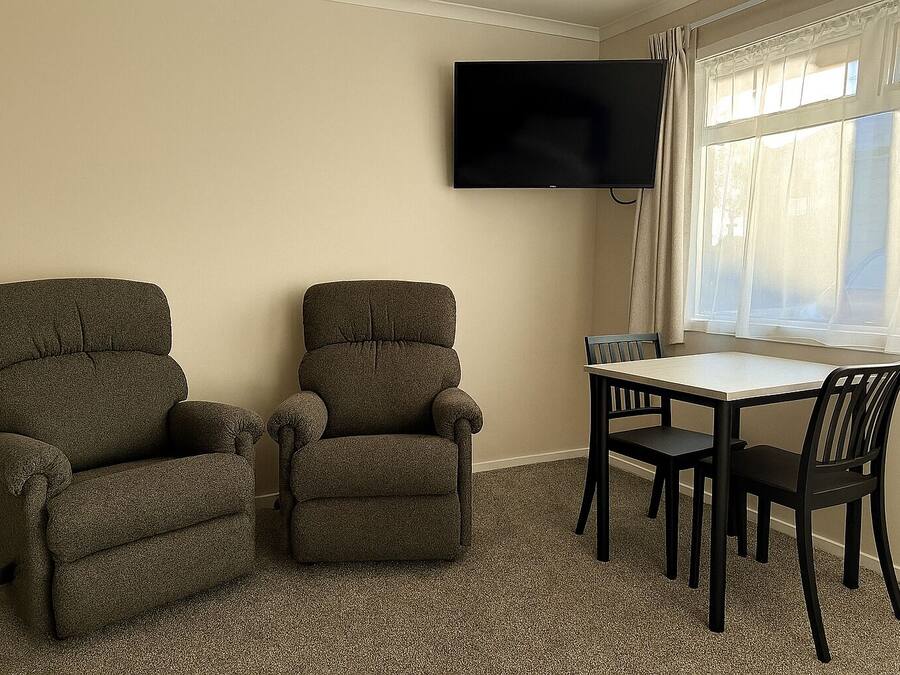 Quarto com duas poltronas, uma mesa pequena e uma televisão fixada na parede.