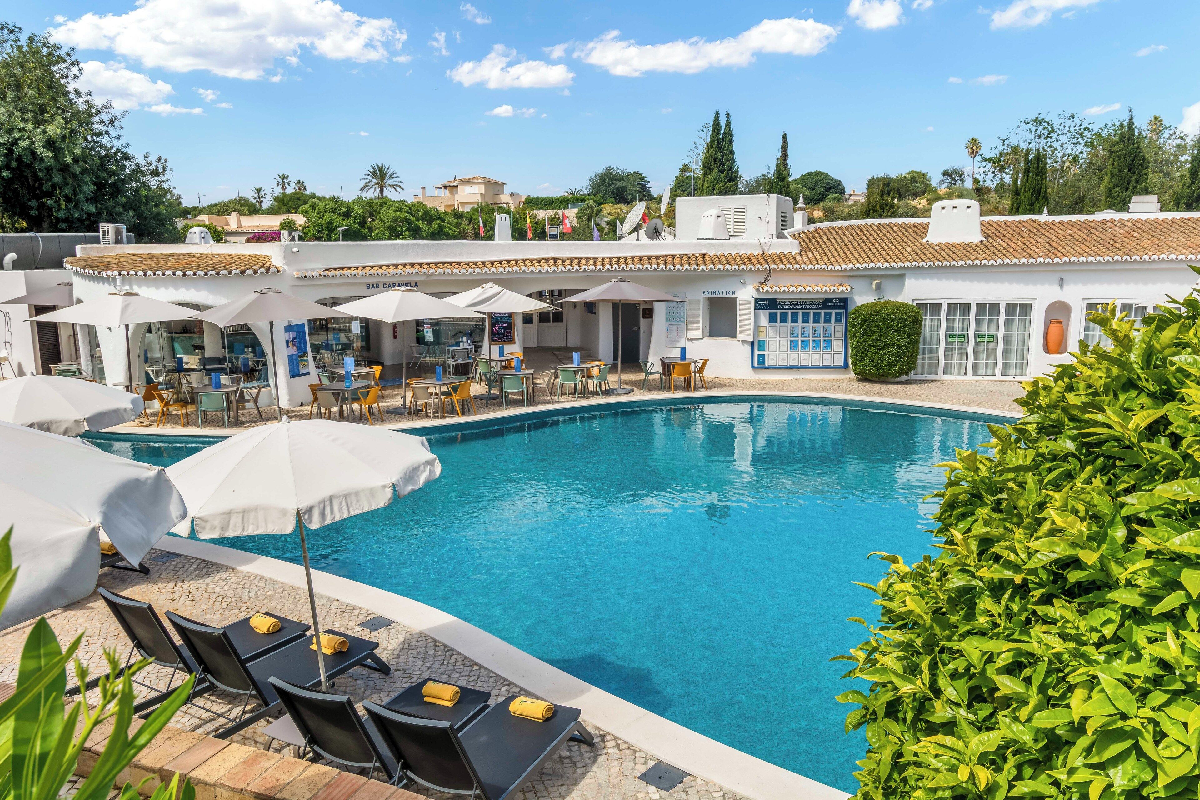 Uma área junto à piscina com espreguiçadeiras, guarda-sóis e um bar.