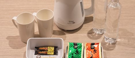 Uma cozinha equipada com cafeteira, duas chávenas, chaleira, duas garrafas de água e um tabuleiro com dois saquinhos de chá e uma caixa de leite condensado.