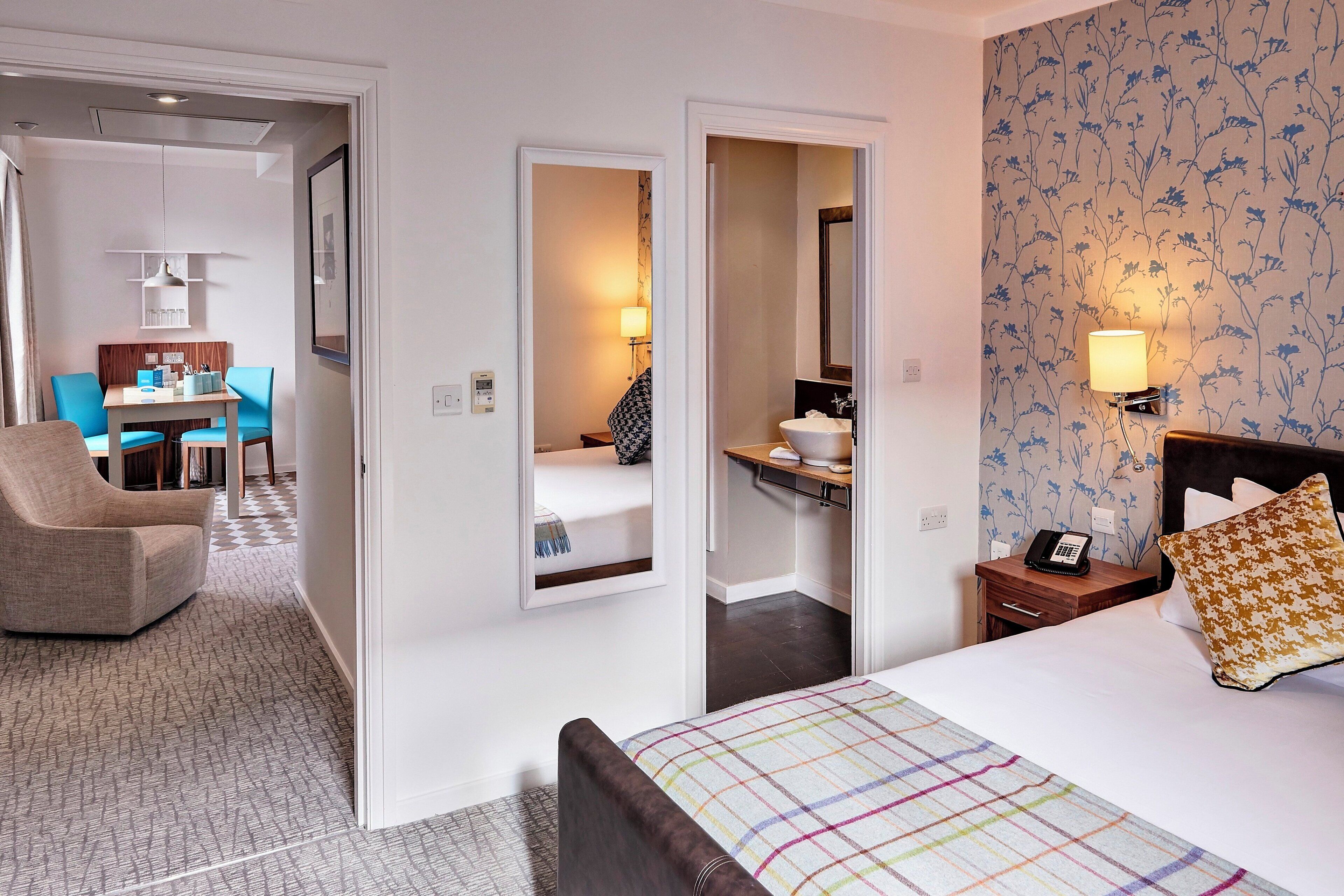 Quarto de hotel com cama, escrivaninha, cadeira e banheiro visível através de uma porta aberta.