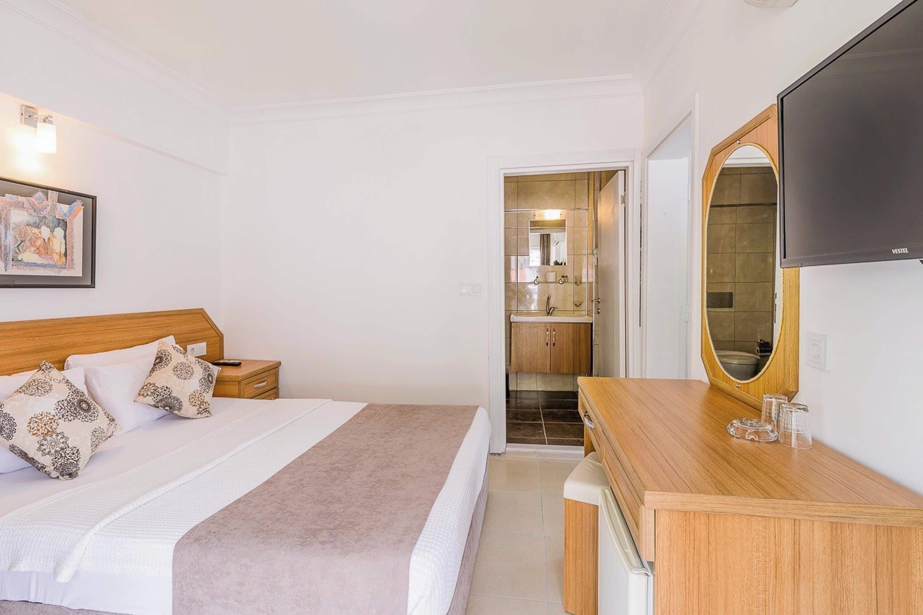 Quarto com cama, mesa de cabeceira e cômoda de madeira com espelho.
