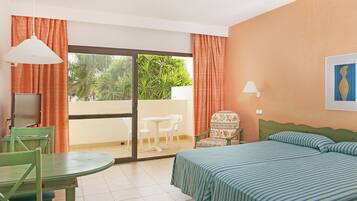Quarto de hotel com cama, escrivaninha, cadeira, televisão e varanda com cortinas.