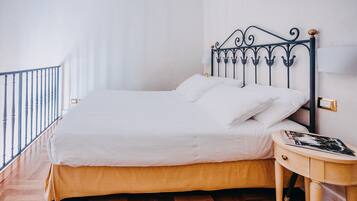 Cama bem arrumada com lençóis brancos, cabeceira de madeira e pequena mesa de cabeceira com abajur.