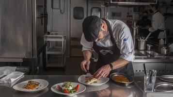 Um cozinheiro preparando comida em uma cozinha profissional, com superfícies de aço inoxidável, um telefone e um carrinho.