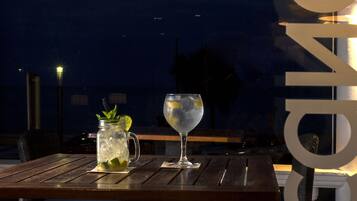 Uma mesa com bebida e um copo, uma cadeira de vime e vista para o céu noturno.