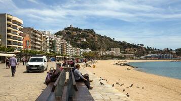 Um calçadão costeiro com bancos, uma praia arenosa e edifícios altos ao fundo.