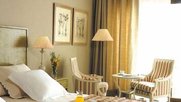 Quarto de hotel com cama, duas cadeiras, uma mesinha e uma bandeja com café da manhã.