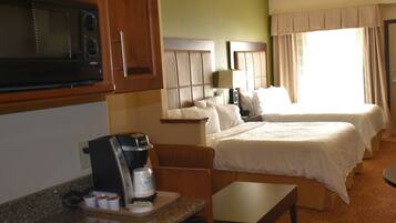 Quarto de hotel com cozinha compacta, uma cama, mesa de cabeceira e janela com cortinas.