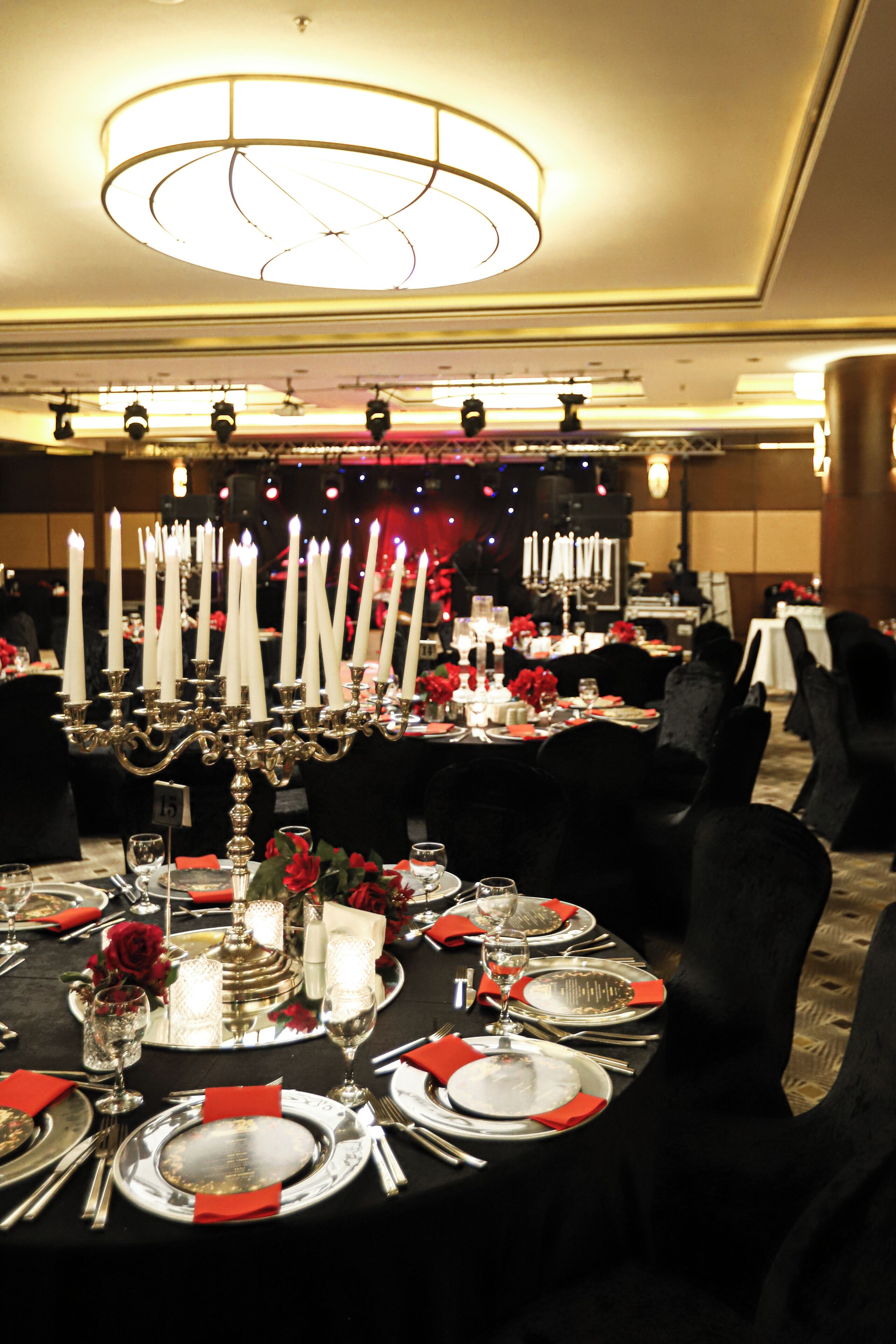 Uma sala de banquetes com mesas montadas para um evento formal, com candelabros, rosas vermelhas e elegantes louças.