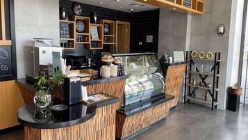 Uma cafeteria moderna com balcão de madeira, máquina de café e vitrine com doces.