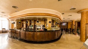 Uma área de bar com balcão curvo, banquetas e uma tela de televisão.