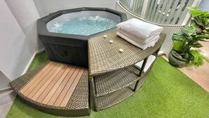 Uma área de spa com hidromassagem, uma cadeira de vime e um pequeno degrau de acesso à banheira.