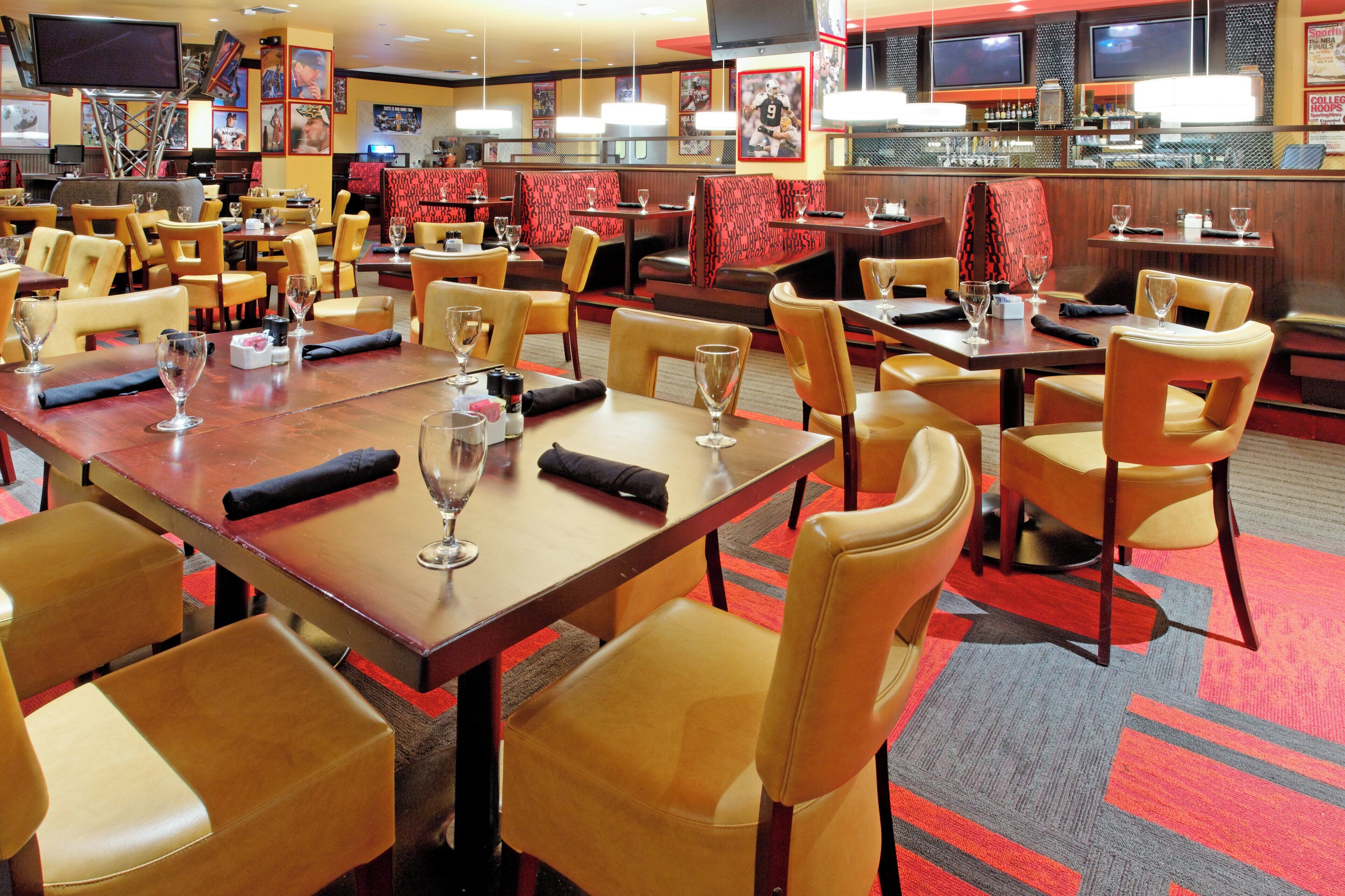 Restaurante com várias mesas e cabines, equipado com copos e talheres, e objetos de coleção esportiva nas paredes.