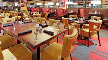 Restaurante com várias mesas e cabines, equipado com copos e talheres, e objetos de coleção esportiva nas paredes.
