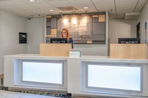 Uma receção com um ecrã digital, uma placa a indicar 'The Hospitality Inn Express Suites' e uma placa a dizer 'Thank You Rewards'.
