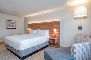 Quarto de hotel com uma cama grande, mesas de cabeceira, uma luminária na parede e uma poltrona estampada.