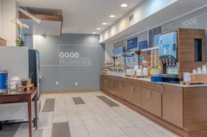 Uma área de café da manhã moderna com um letreiro 'Bom dia', uma máquina de café e diversas opções de alimentos.