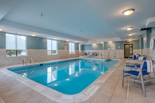 Uma grande piscina interior com água azul cristalina, rodeada por paredes azulejadas em azul e branco, e equipada com várias áreas de estar e uma porta que dá para outro espaço.