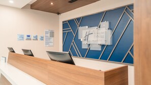 Bancada de recepção de hotel com design moderno, incluindo um painel de parede geométrico azul e um balcão de madeira.