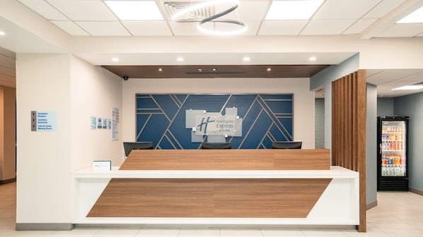 Uma receção com um design de parede geométrico azul e branco, um sinal da Holiday Inn Express e um frigorífico com bebidas.