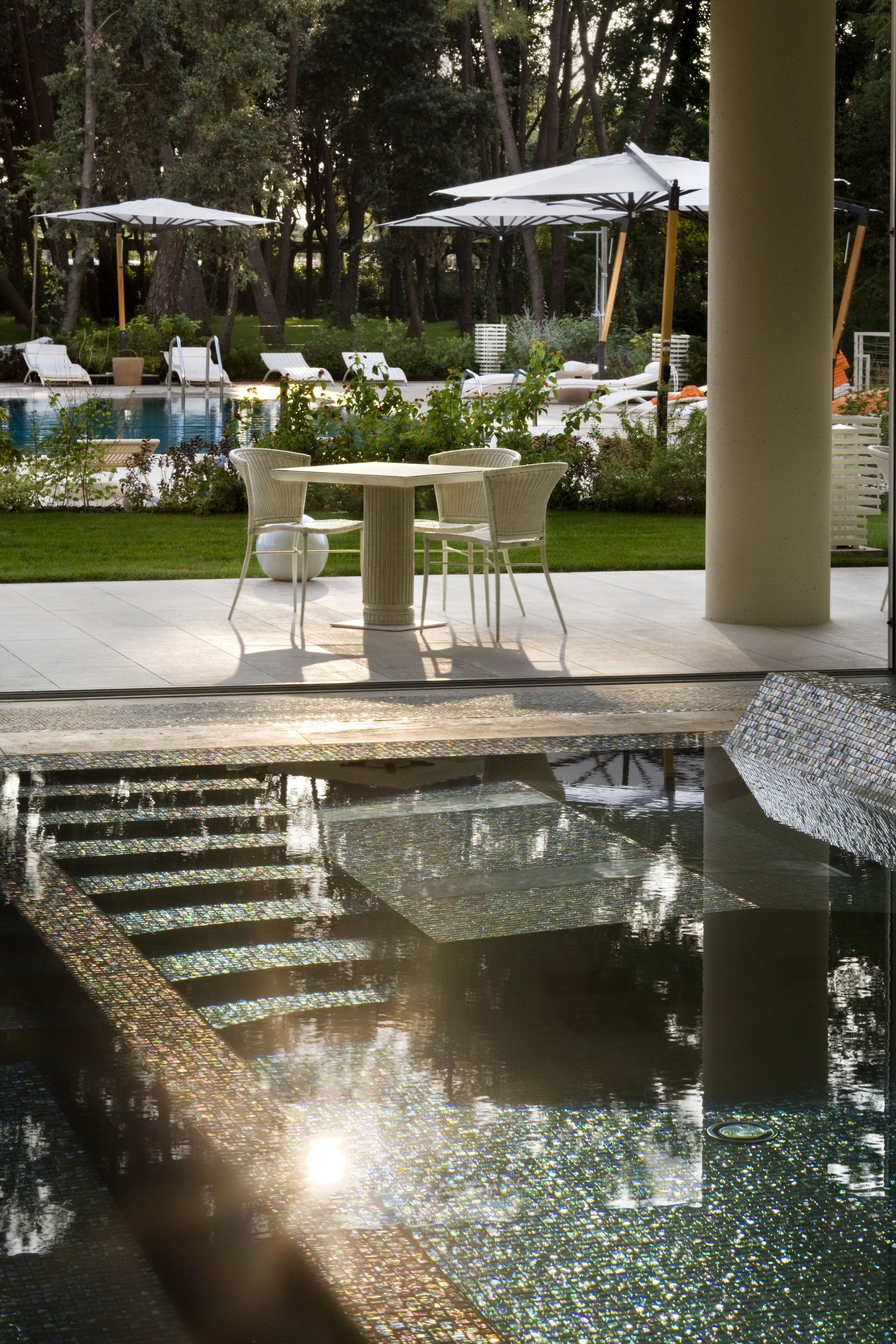 Área de piscina com espreguiçadeiras, guarda-sóis e uma mesa com cadeiras.
