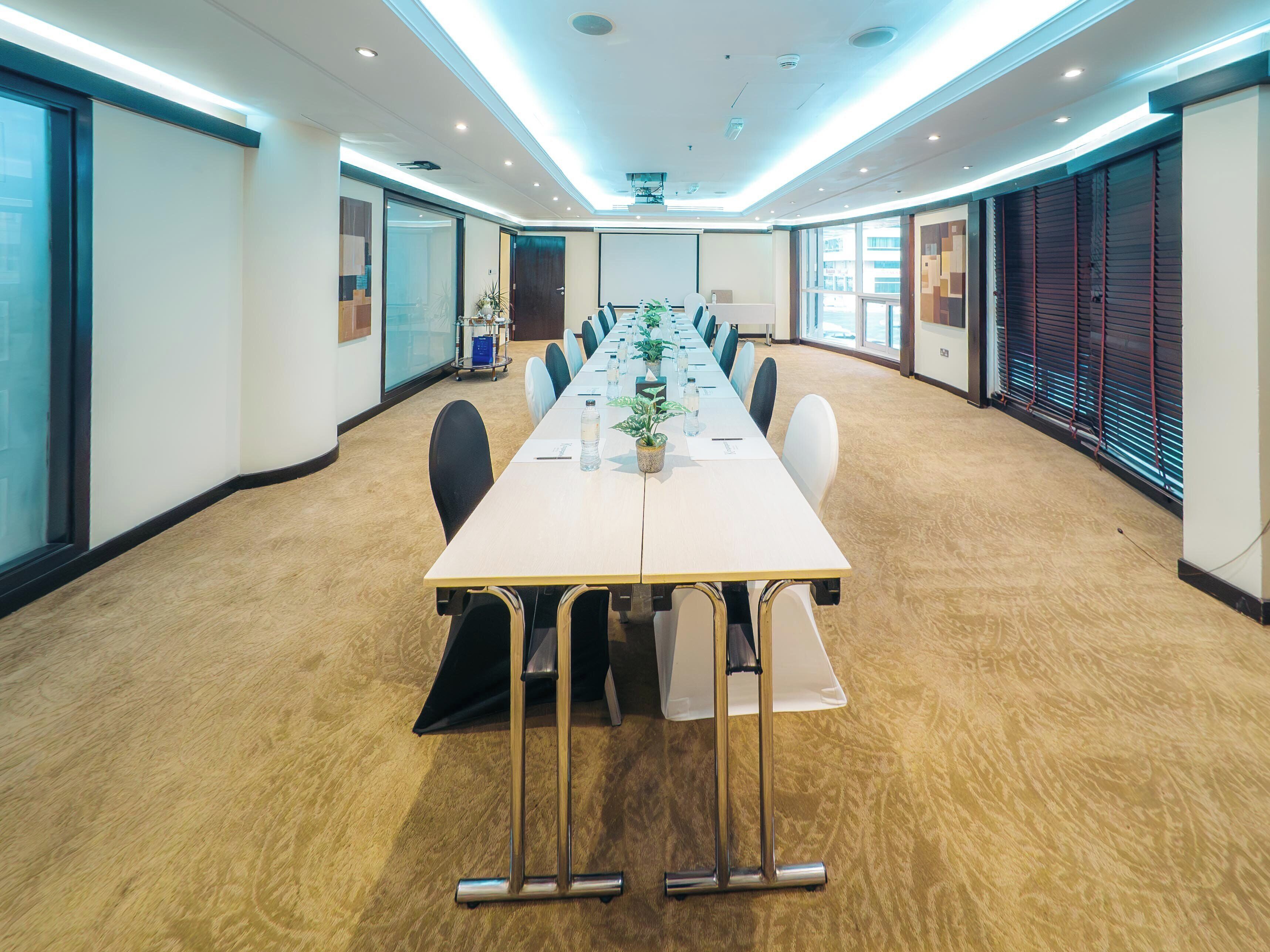 Uma sala de conferências com uma mesa comprida, cadeiras e uma tela de projetor.