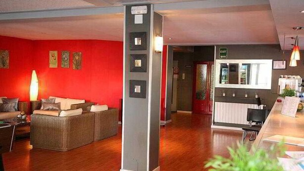 Um hall de hotel com balcão de recepção, área de estar com sofás e uma parede vermelha com obras de arte emolduradas.