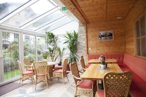 Um restaurante com interior em madeira, grandes janelas e vista para o jardim.
