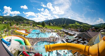 Um parque aquático com várias piscinas e toboáguas, cercado por colinas verdes e edifícios.