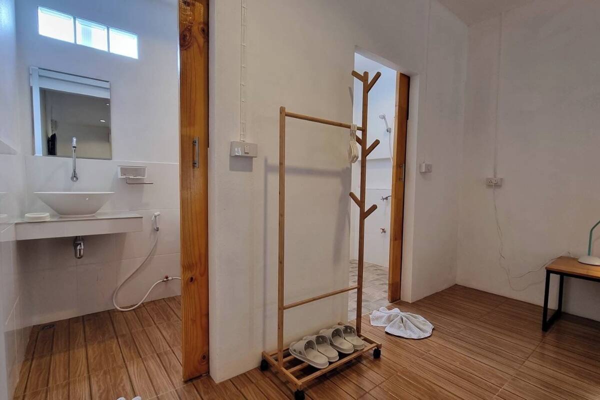 Quarto com piso de madeira, pia branca com espelho, cabideiro de madeira, um banco e uma mesa com abajur.