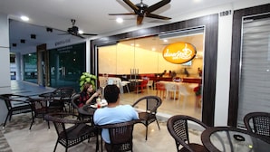 Um espaço de refeições em ambiente interno com cadeiras e mesas de vime, um ventilador de teto e vista para um restaurante chamado 'diners cafe'.