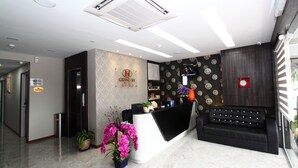 Uma área de recepção de hotel com design moderno, incluindo um balcão de recepção, um sofá e uma parede com padrão circular.