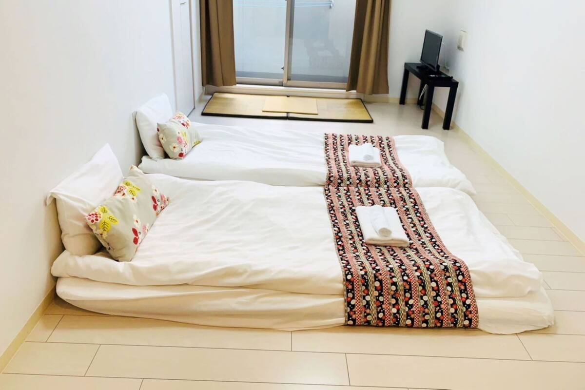 Quarto de hotel com duas camas, uma mesinha, uma televisão e vista para o exterior.