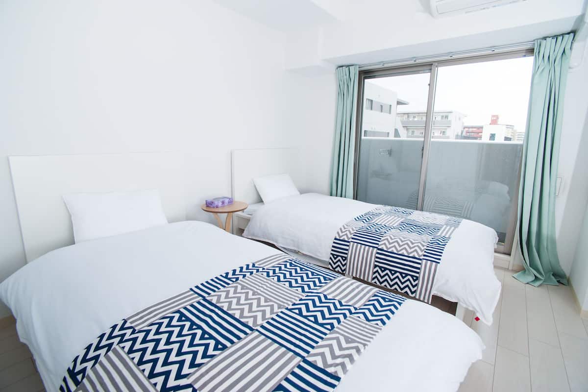 Quarto de hotel com duas camas, uma mesinha e uma janela com cortinas.