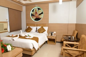 Quarto de hotel com uma cama, uma mesa pequena, uma cadeira, ar condicionado fixado na parede e uma flor decorativa na mesinha de cabeceira.