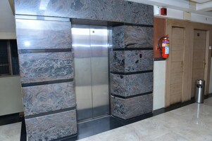 Elevador moderno com acabamento metálico, paredes de mármore e extintor fixado na parede.