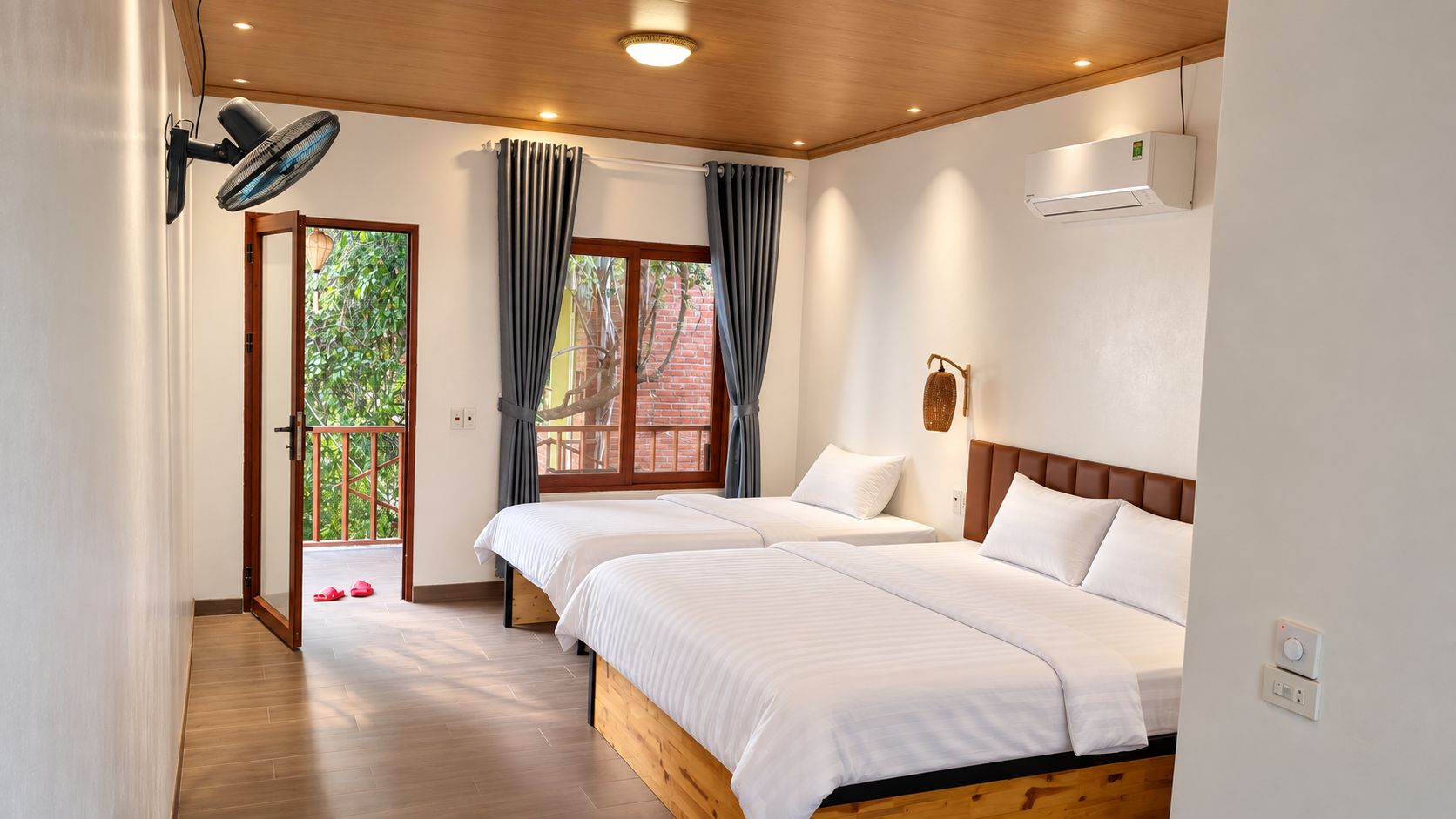 Quarto de hotel com duas camas, ventoinha no teto, ar condicionado e varanda com vista para o verde.