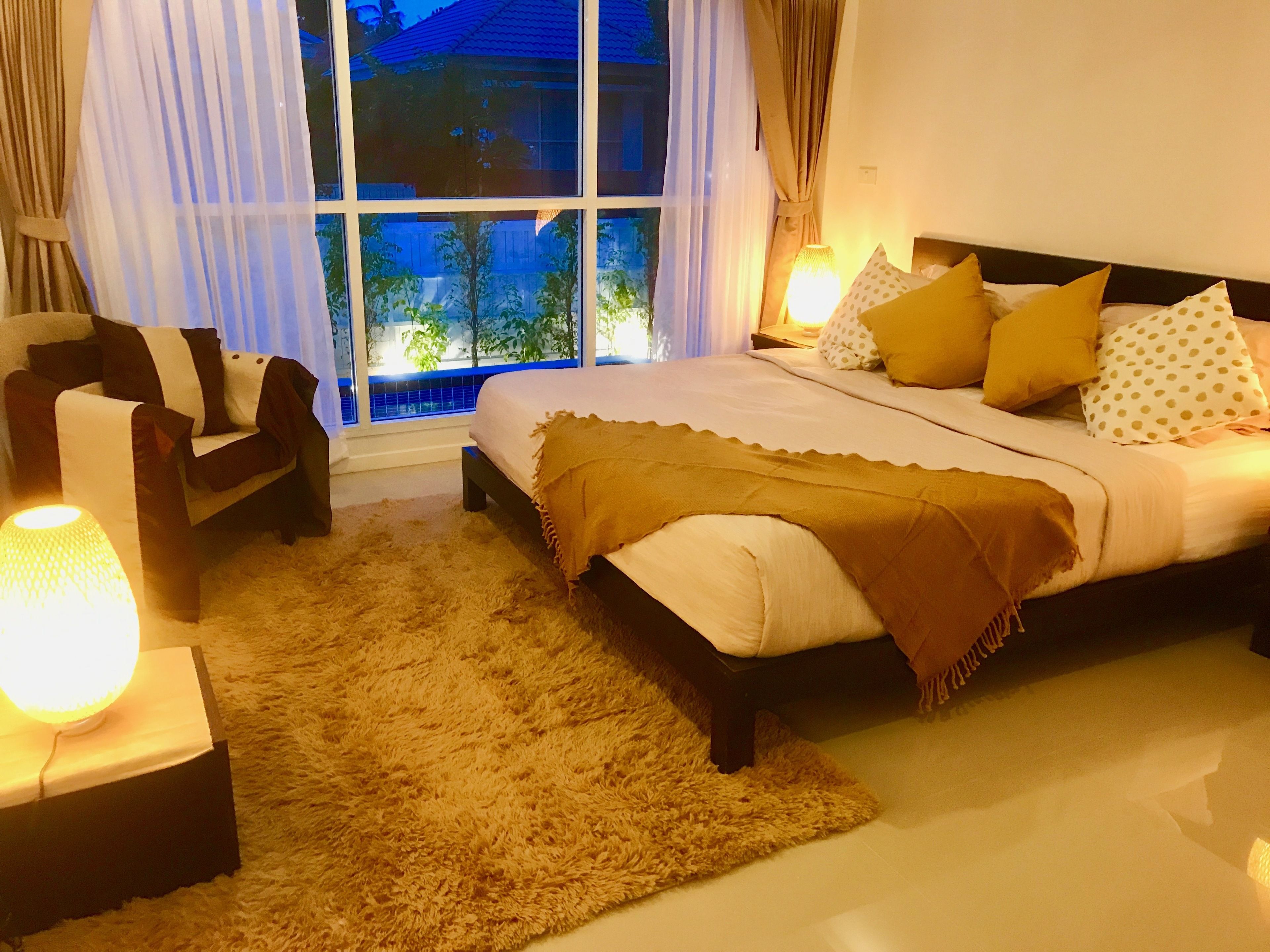 Quarto com uma cama grande, uma cadeira, mesa de cabeceira e janela com cortinas.