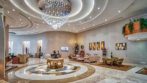 Um hall amplo com piso circular estampado, um candelabro e um espaço de estar com sofás e uma mesa de centro.