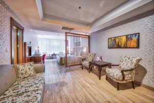 Uma sala de estar espaçosa com piso de madeira, um sofá, uma poltrona florida e uma mesa de jantar.