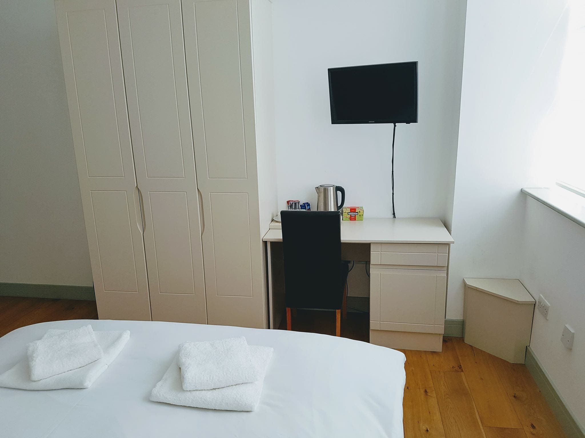 Quarto de hotel com uma cama, uma escrivaninha com cadeira, uma televisão e um cesto de lixo.