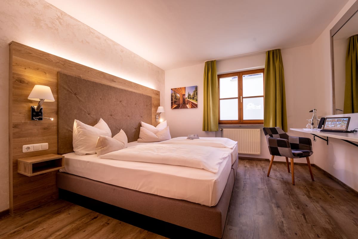 Quarto de hotel com uma cama grande, uma escrivaninha com computador, uma cadeira e janela com cortinas.