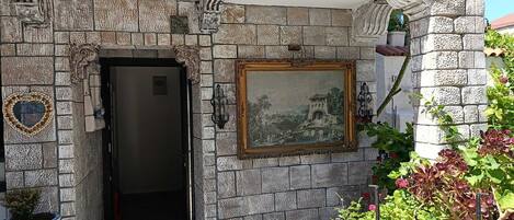 Fachada de pedra com um quadro emoldurado, uma porta e plantas em vasos.