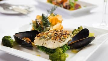 Prato de frutos do mar com mexilhões e peixe, acompanhado de brócolis e um copo de vinho.